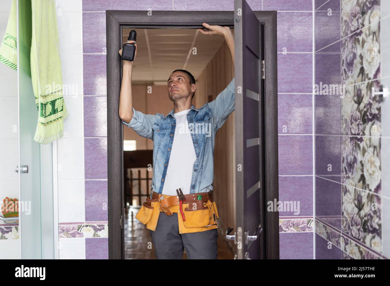 Young handyman installing a white door with an electric hand drill in a ...
