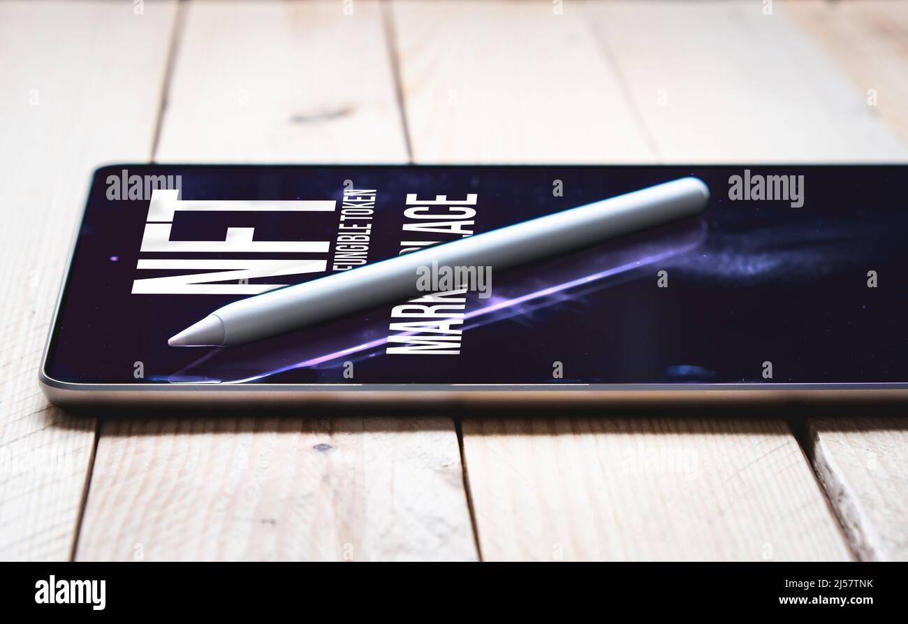 Tablet with pen on wooden table with a wallpaper of an NFT marketplace ...