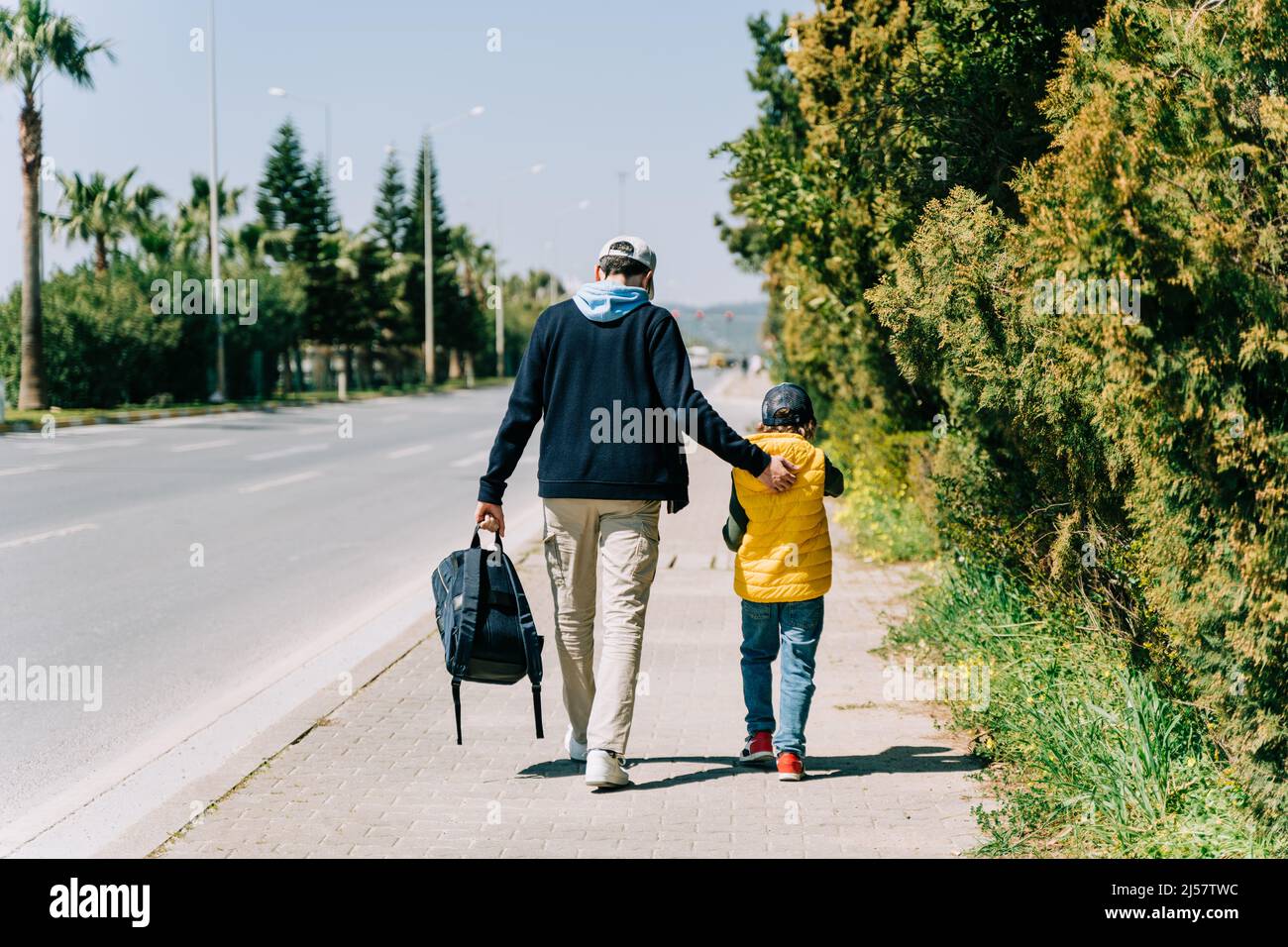 Rearview of father and son walking near city road. Dad holding his kid ...