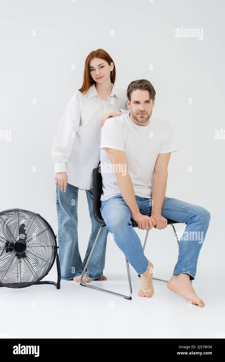 Young woman in shirt and jeans standing near boyfriend on chair on ...