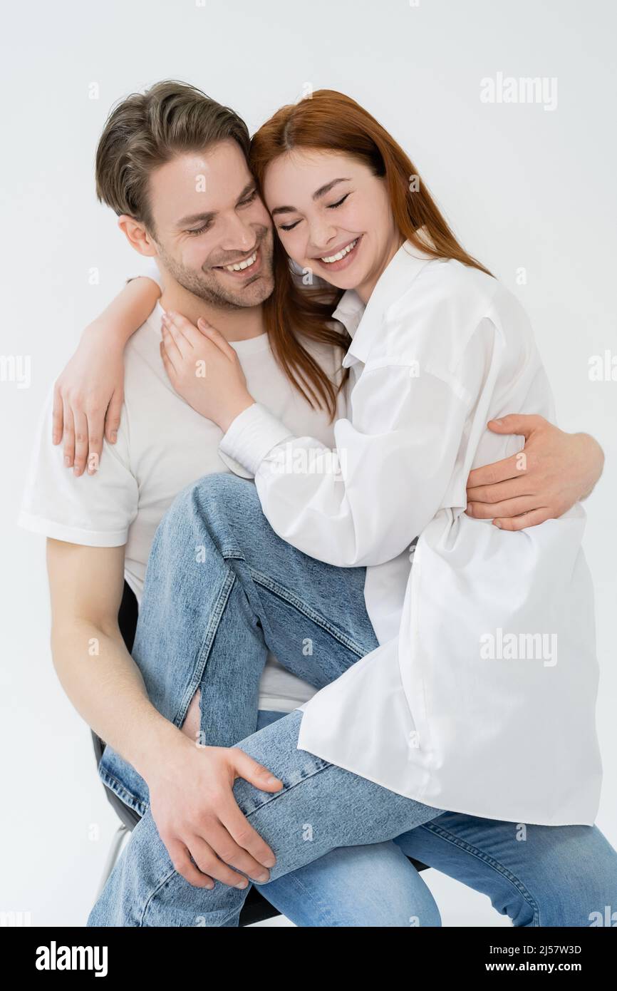 Positive couple hugging while sitting on chair isolated on white Stock ...