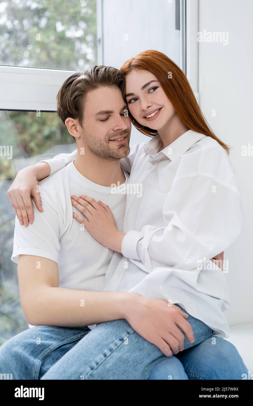 Cheerful woman in shirt hugging boyfriend near window at home Stock ...