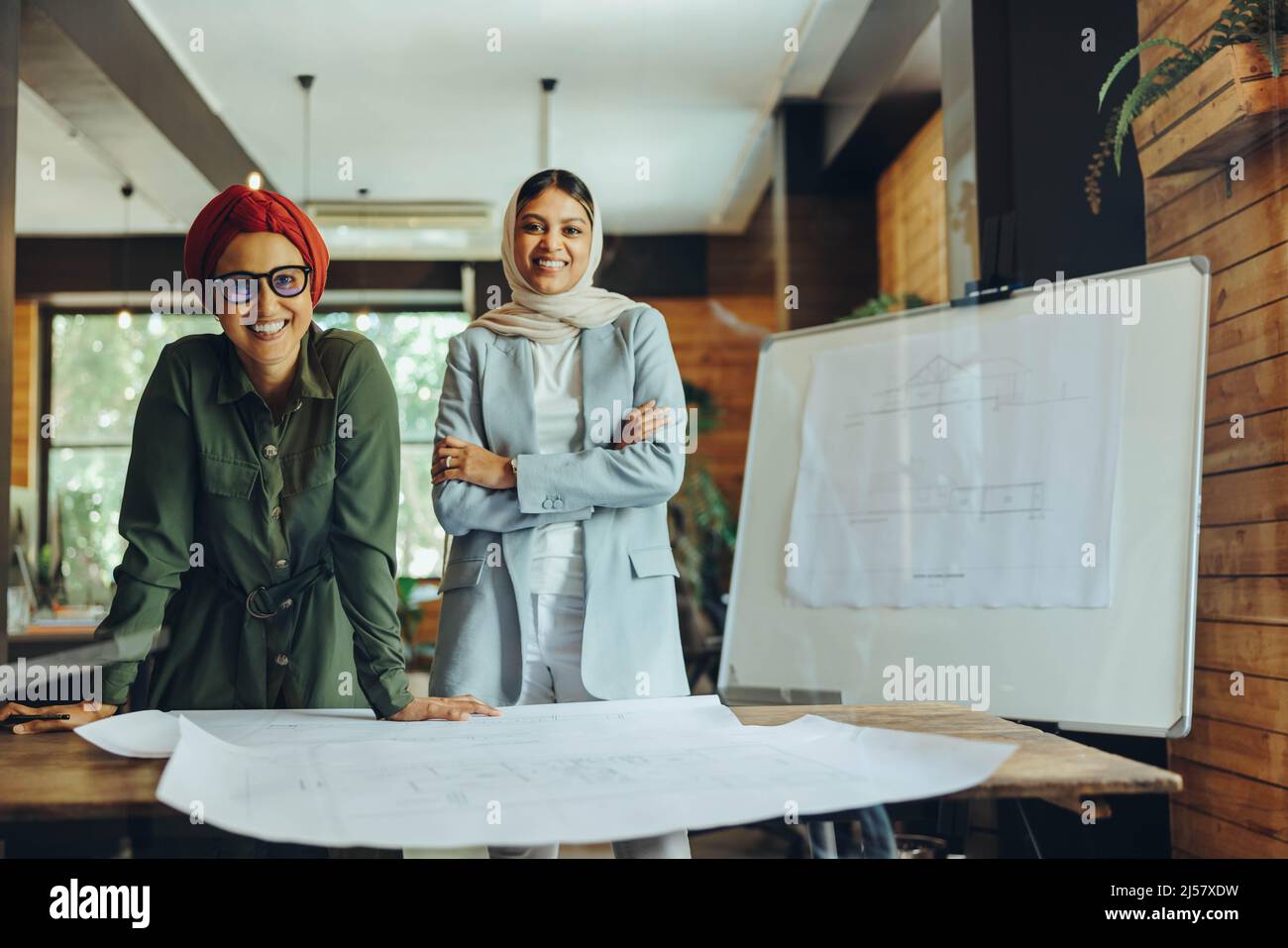 Happy Muslim designers smiling at the camera while working on blueprint drawings. Two creative ...