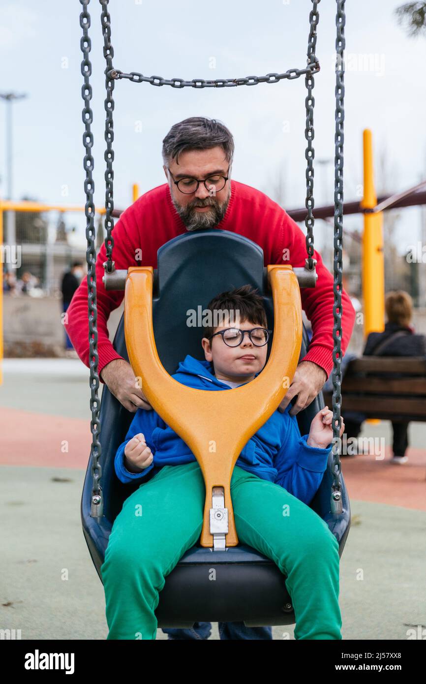 Man pushing his son with disability on an adapted swing for people with ...