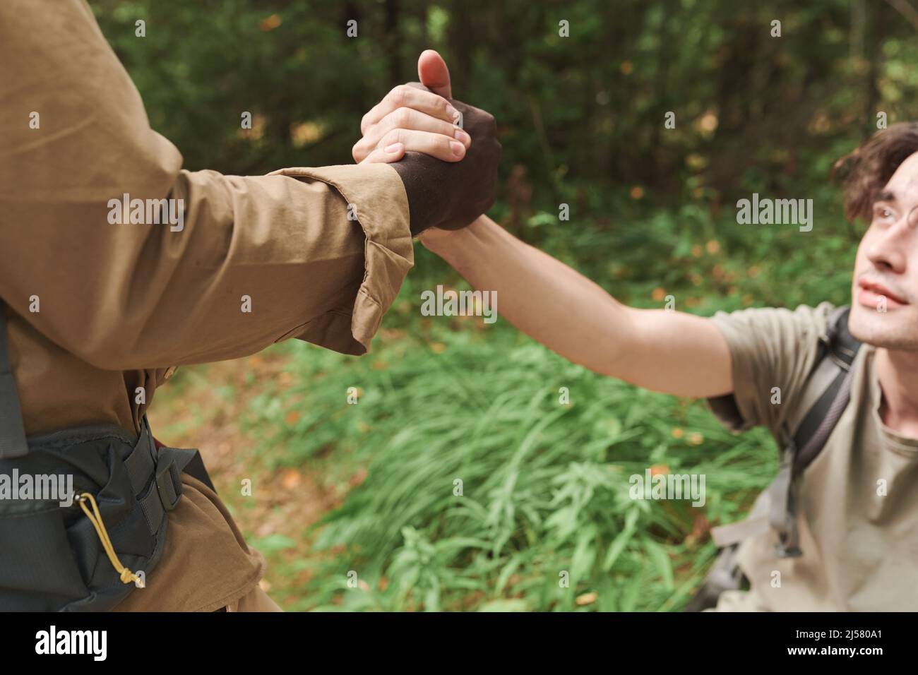 Close-up of black man holding hand of friend while helping him to hike ...