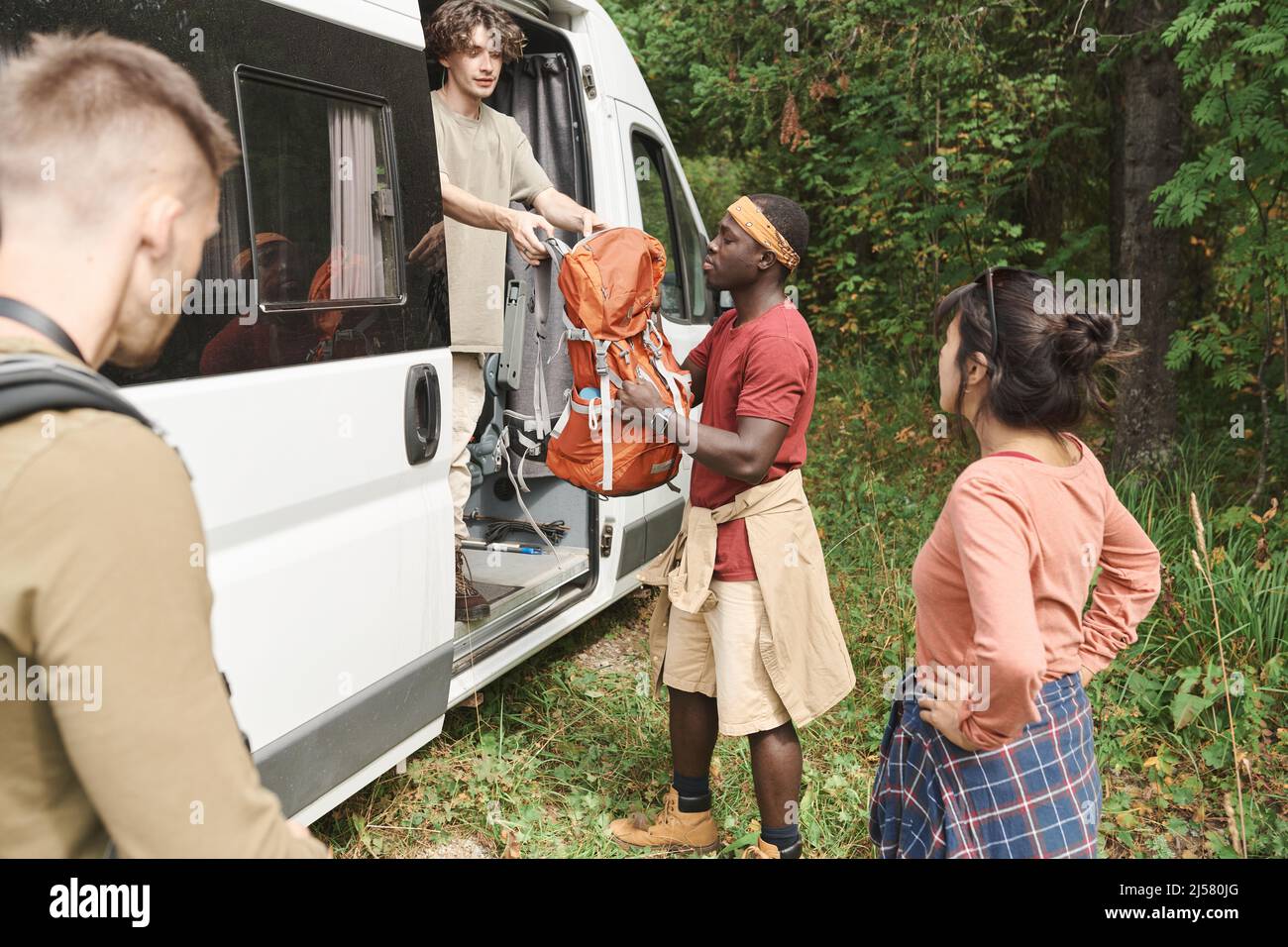 Young male hiker giving backpack to black friend while getting out of ...