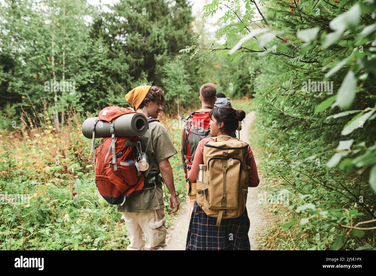 Rear view of young people with backpacks walking along path in forest ...