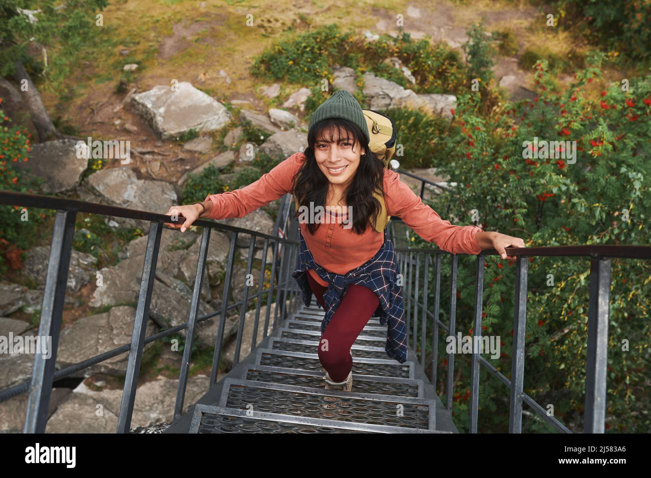 Portrait of positive young mixed race hiker in hat wearing backpack ...
