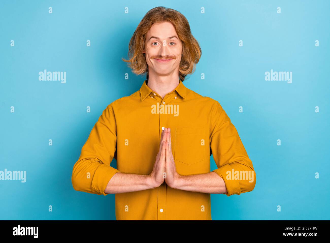 Portrait of attractive cheerful funky long-haired guy praying namaste ...