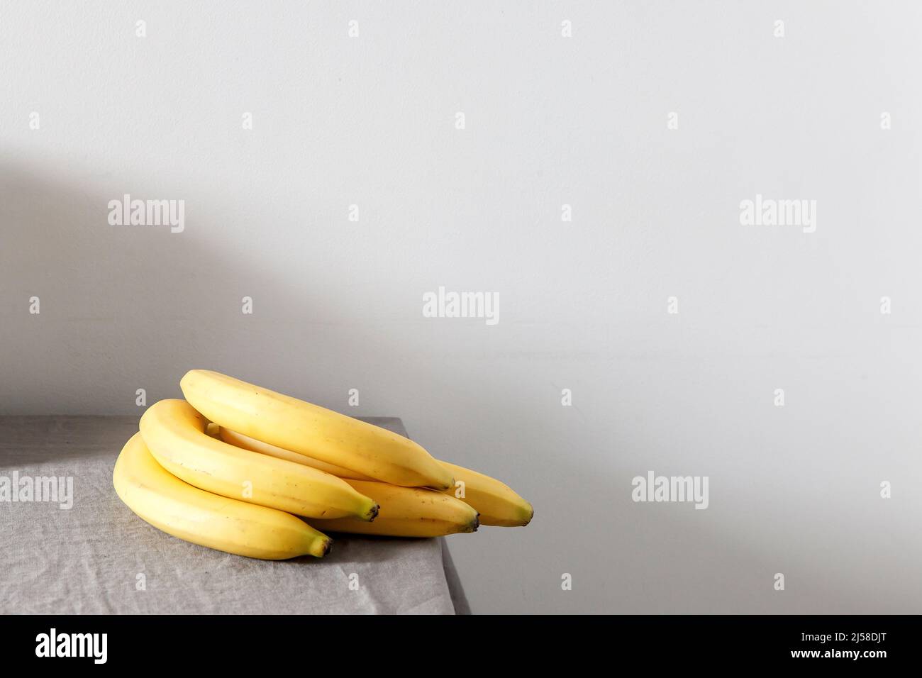 A bunch of bananas on a beige table against a white wall. Scandinavian ...