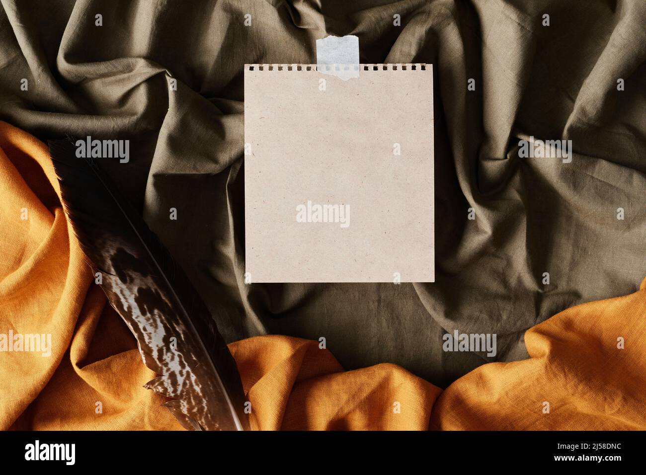 Above view of blank sticky note and feather on wrinkled gray and orange ...
