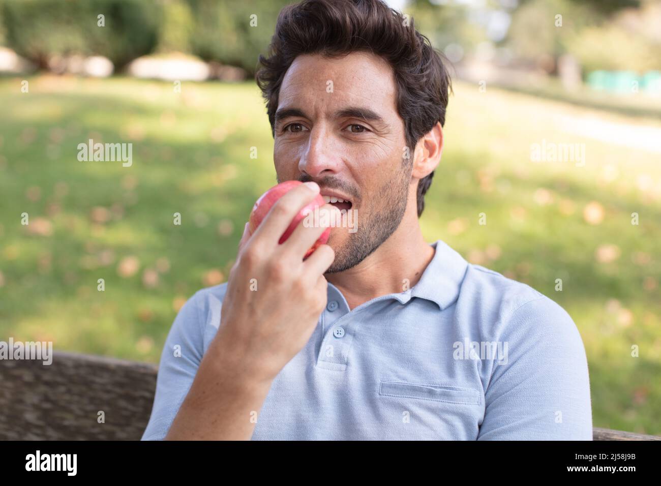 young man is eating apple in park after work Stock Photo - Alamy