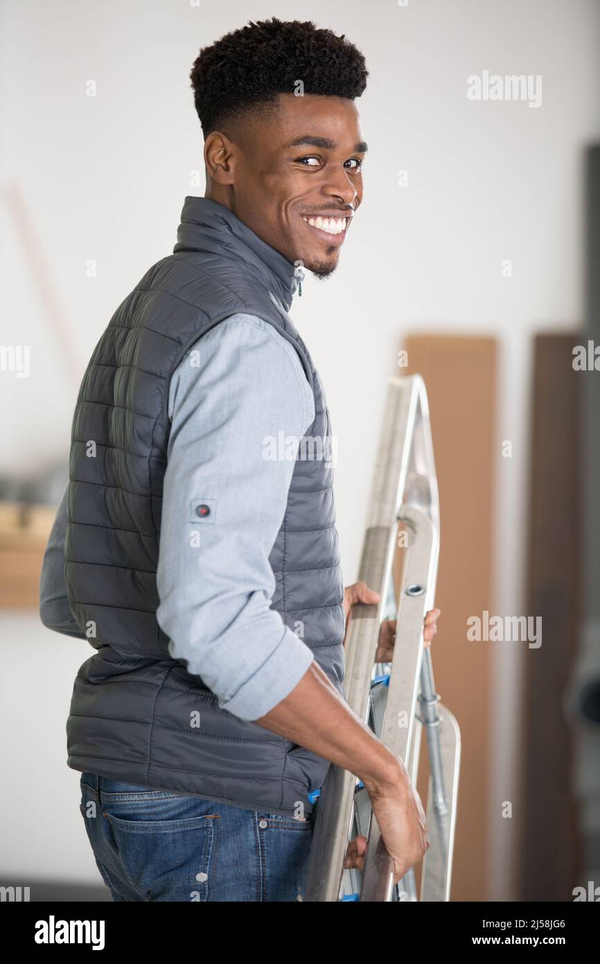 young smiling tradesman carrying a stepladder Stock Photo - Alamy