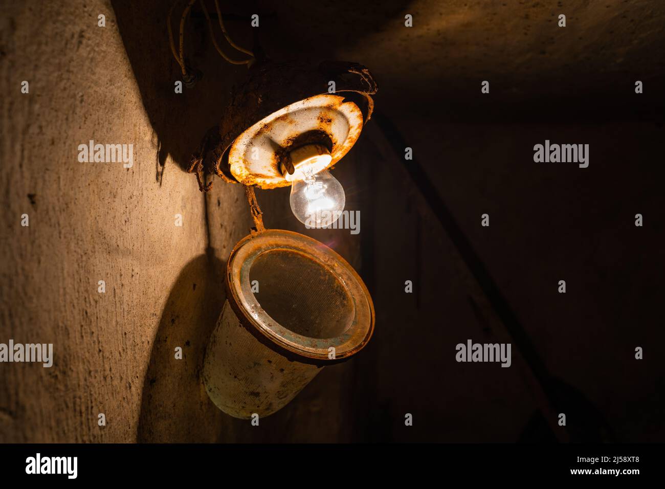 An old incandescent light bulb in an old rusty ceiling lamp in a dark ...