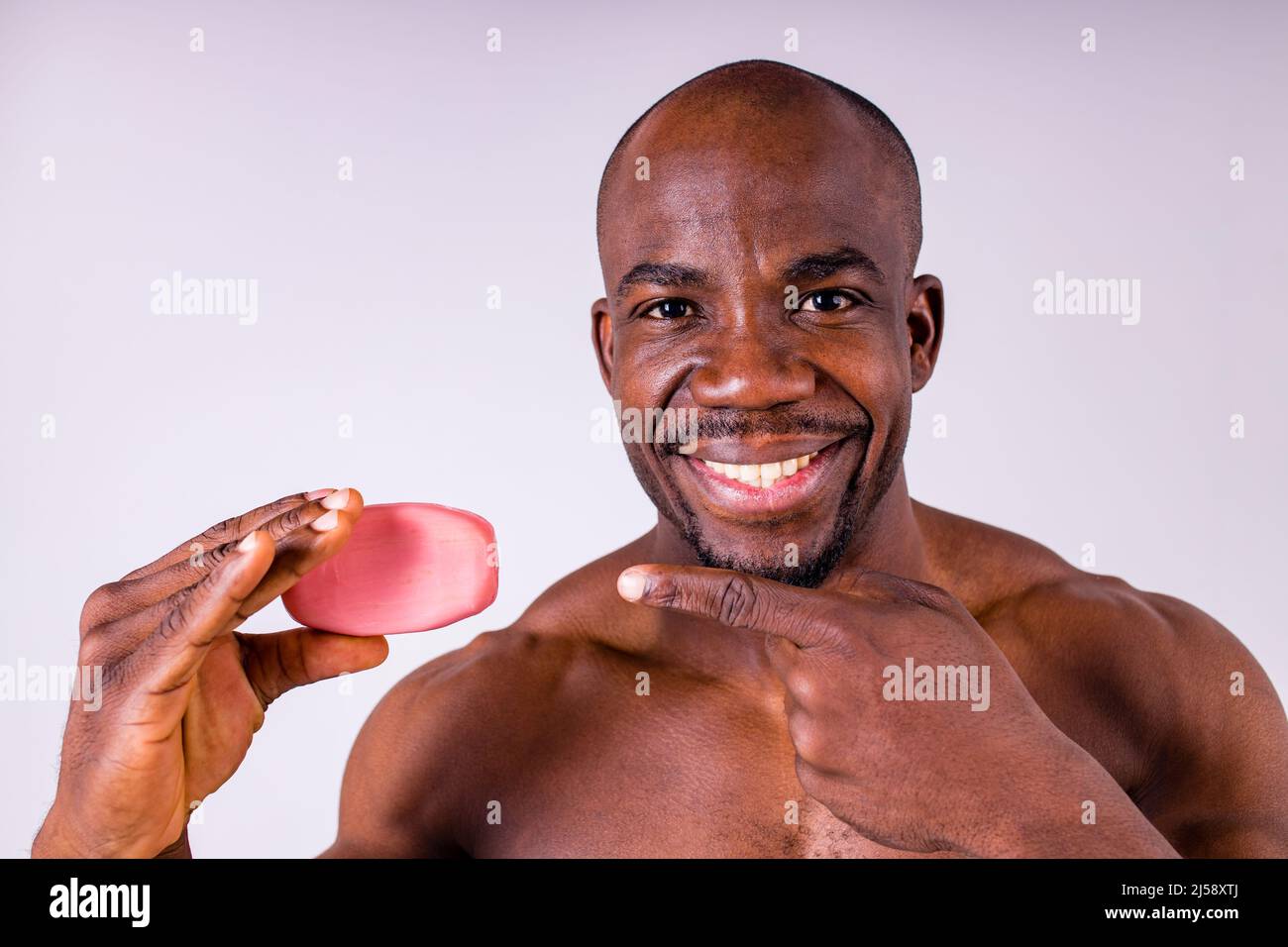 African man holds and show a piece of wet soap in studio white ...