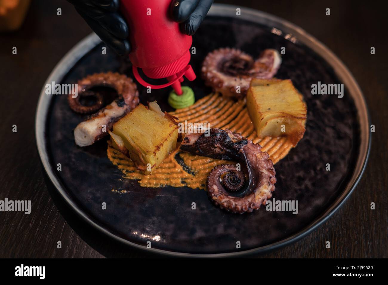 Chef preparing octopus with potatoes on pea mash decorated with edible ...