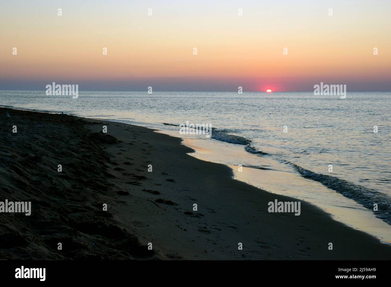 The sun setting beyond the horizon of a calm sea and part of the sandy ...