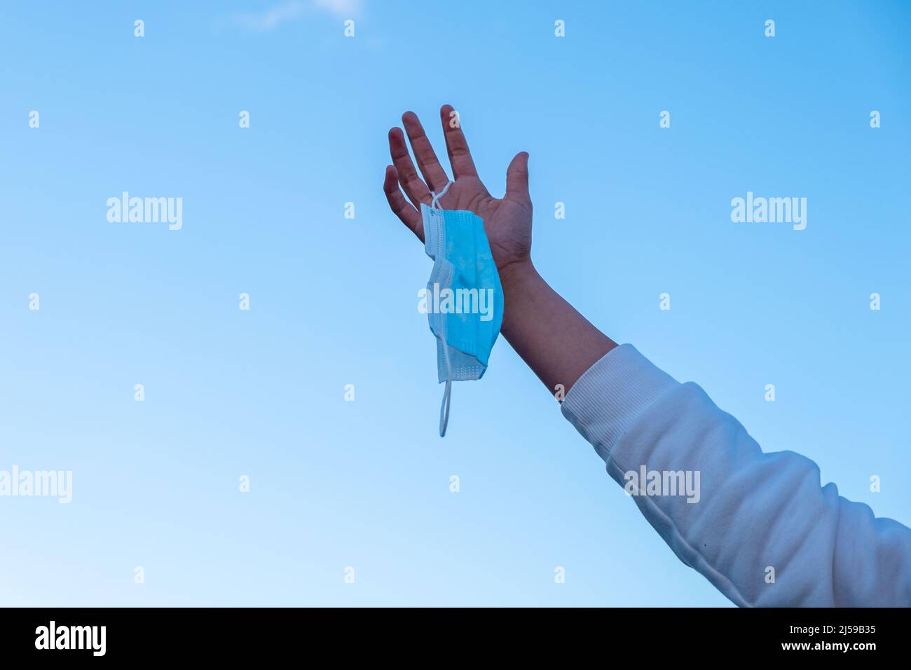 A hand raising a mask with the sky in the background, end of the ...