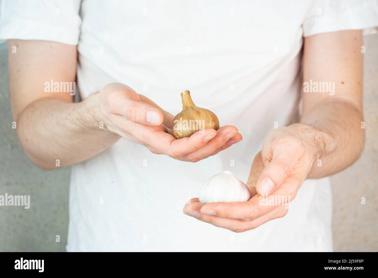 Garlic and fermented garlic in man's hands. A man in a white t-shirt on ...