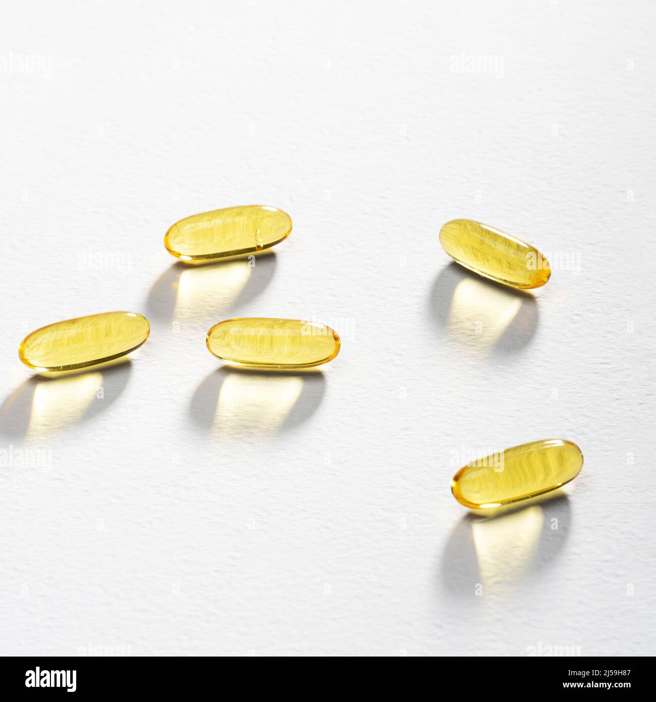 Sunlight passes through a few Omega-3 capsules lying on a white ...
