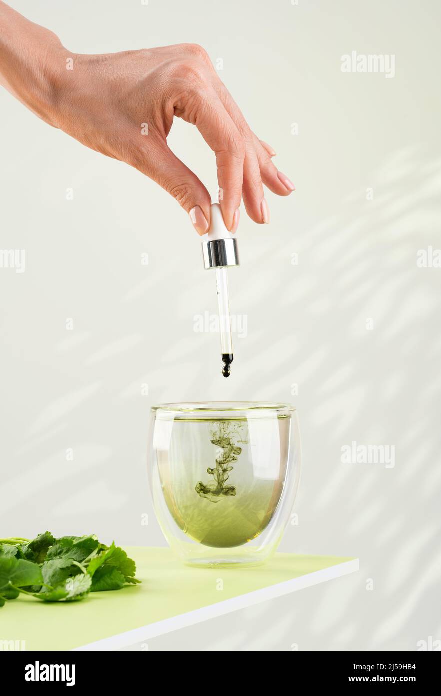 Female hand pours liquid chlorophyll into a glass of water with a ...