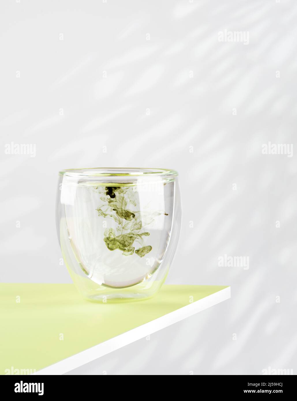 Glass of water with liquid chlorophyll on a green table. Natural light ...
