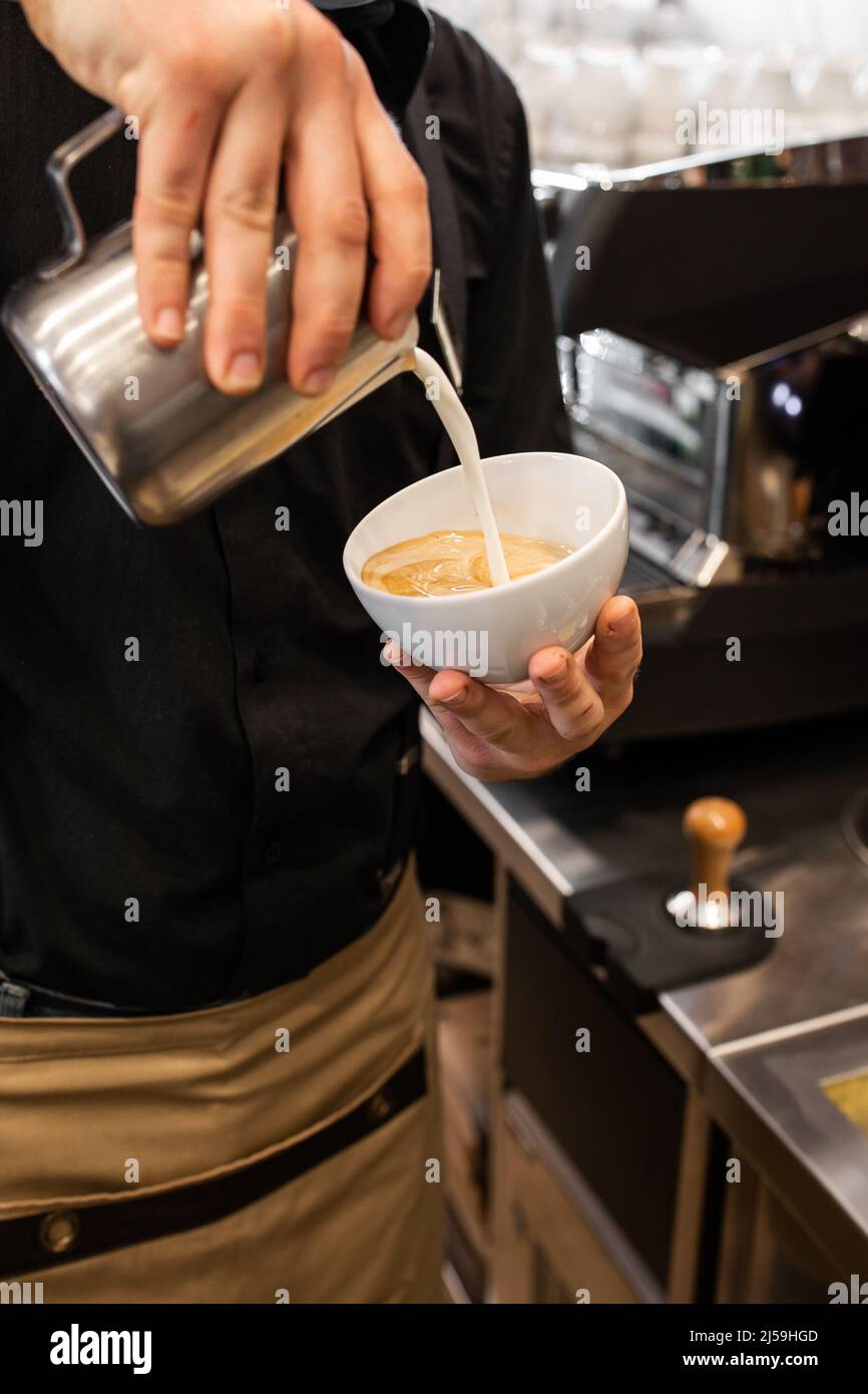 Professional barista pouring steamed milk into coffee glass cup making ...
