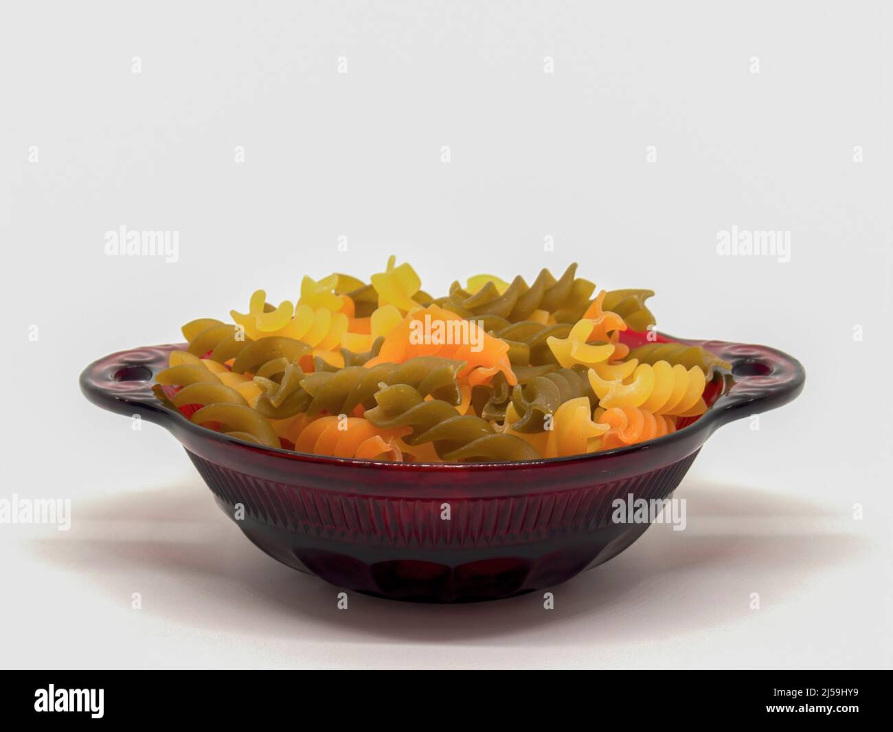 Studio shot of a heap of colorful raw fusilli pasta on a red glass ...
