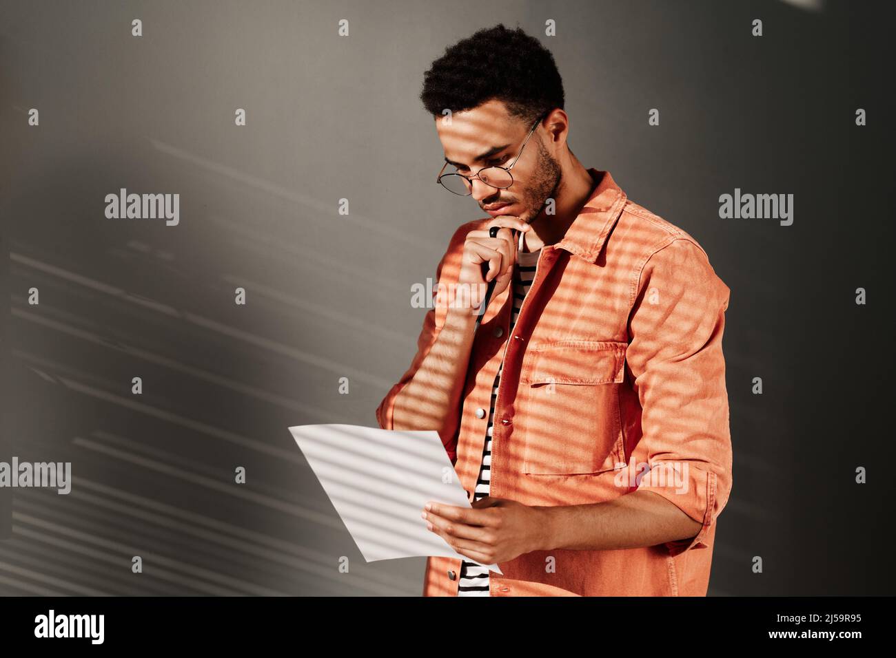 Serious busy young black man with beard touching chin while analyzing ...