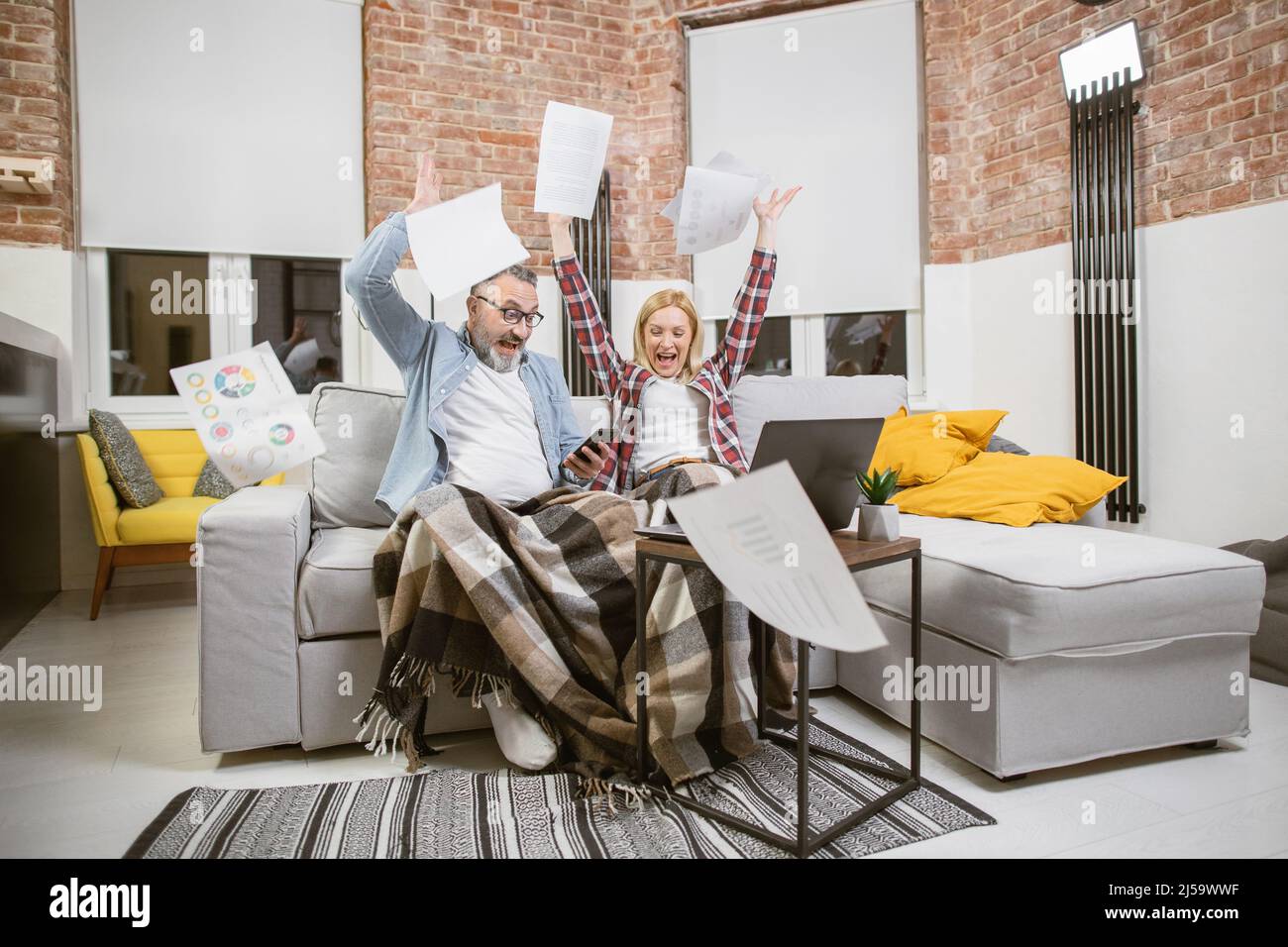Cheerful mature man and woman throwing paper around after successful ...