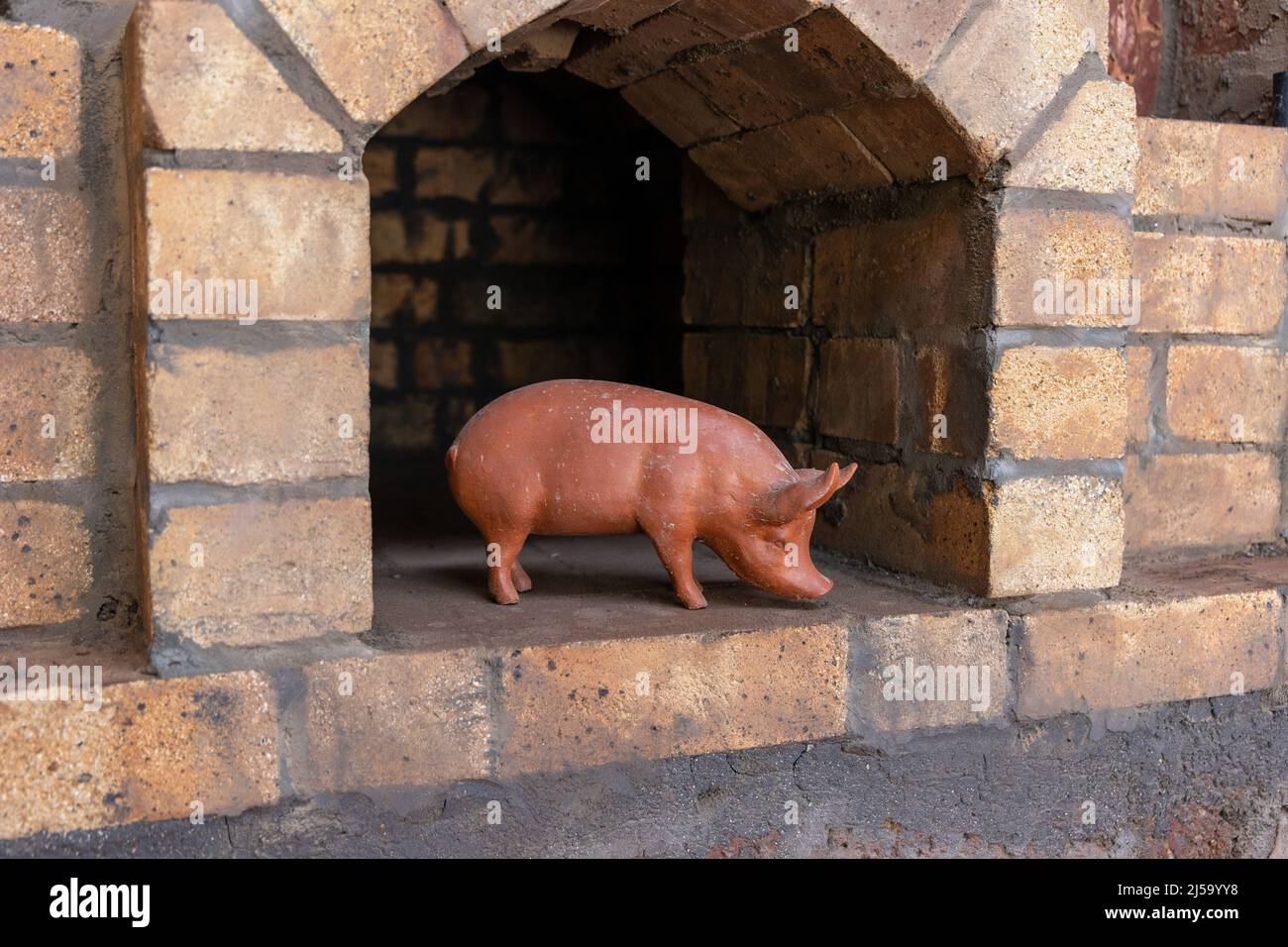 Porcelain statue of a pig kept in front of a traditional brick furnace ...