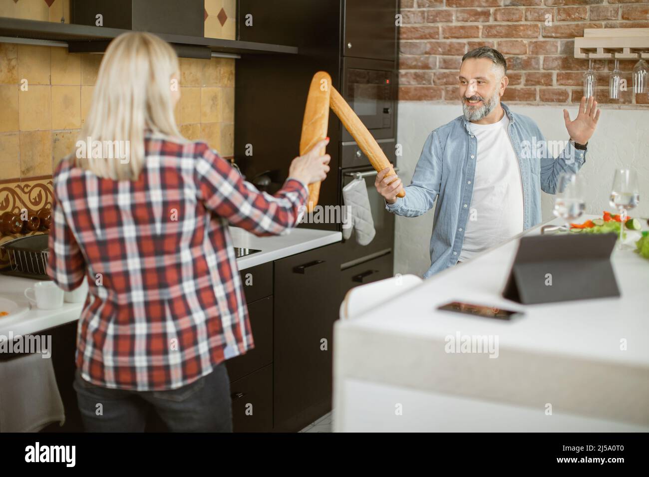 Joyful mature man and woman fighting with baguettes like as swords ...