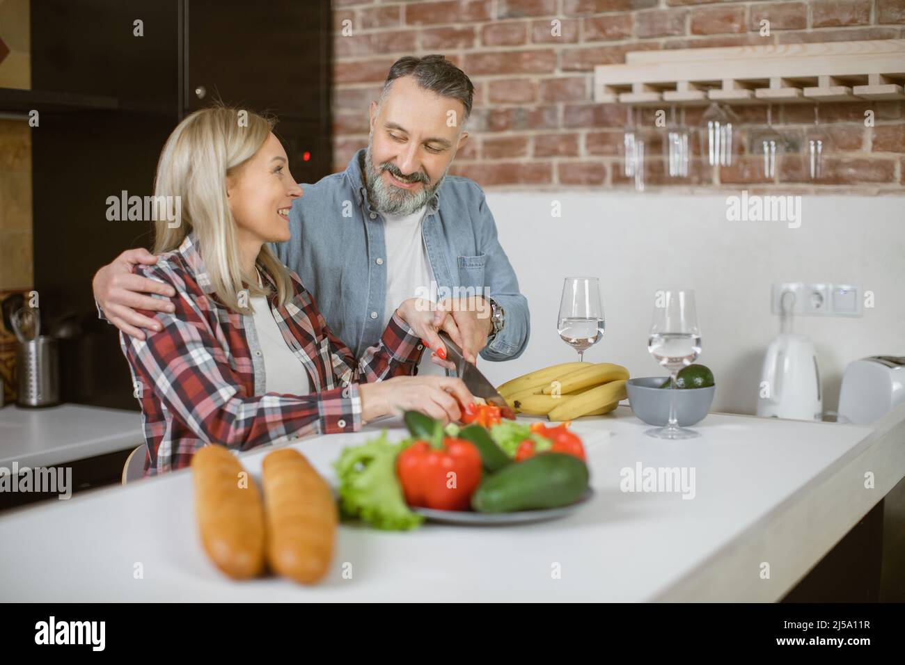Handsome mature man and charming woman enjoying cooking process at ...