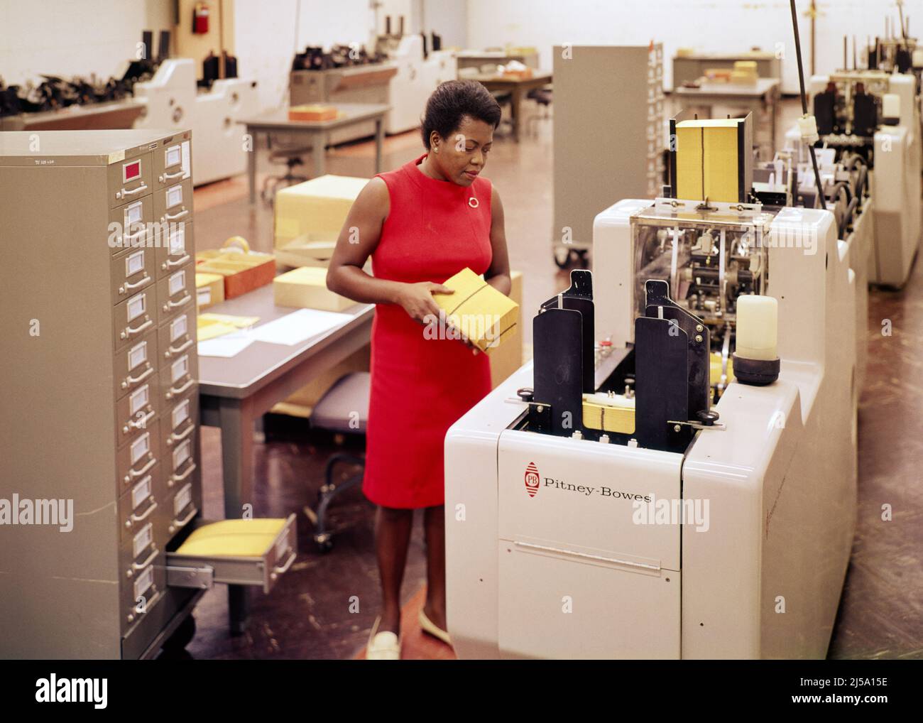 1960s AFRICAN-AMERICAN WOMAN WORKING OPERATING A MAILING MACHINE AT A ...