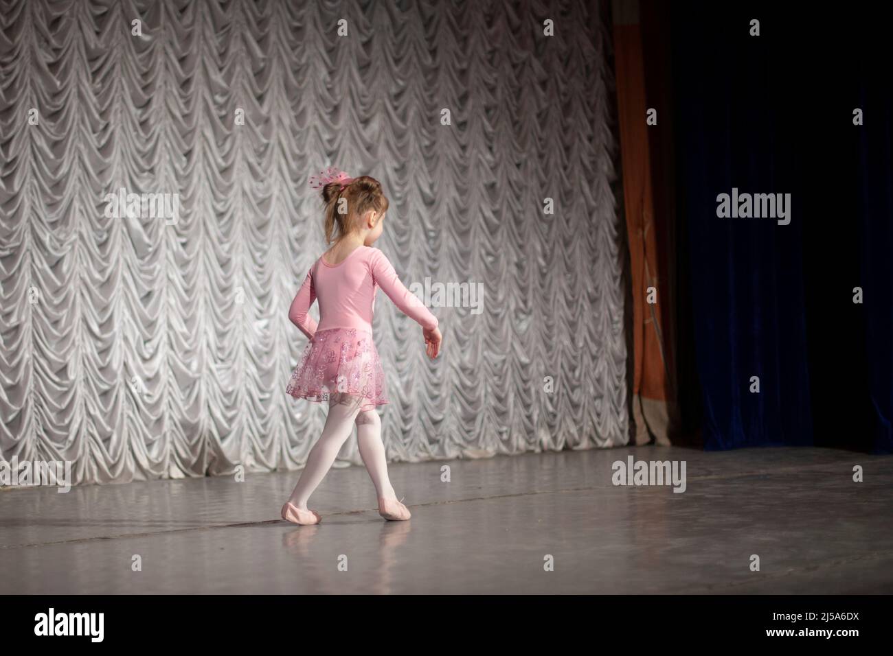 A girl in a pink dress is dancing on the stage. A child from a dance ...