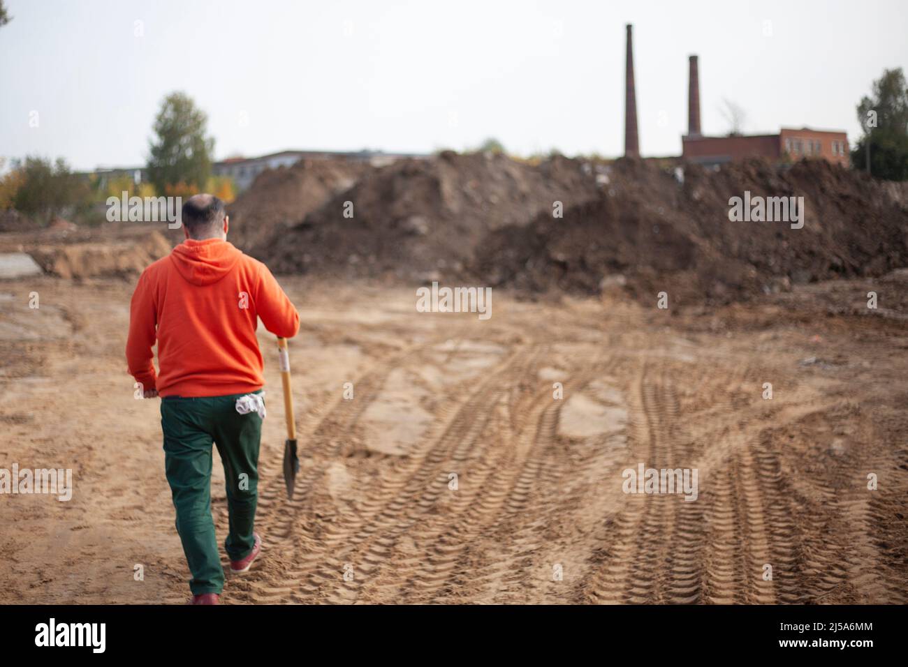 Man with shovel walks on ground. Worker on construction site. Place of ...