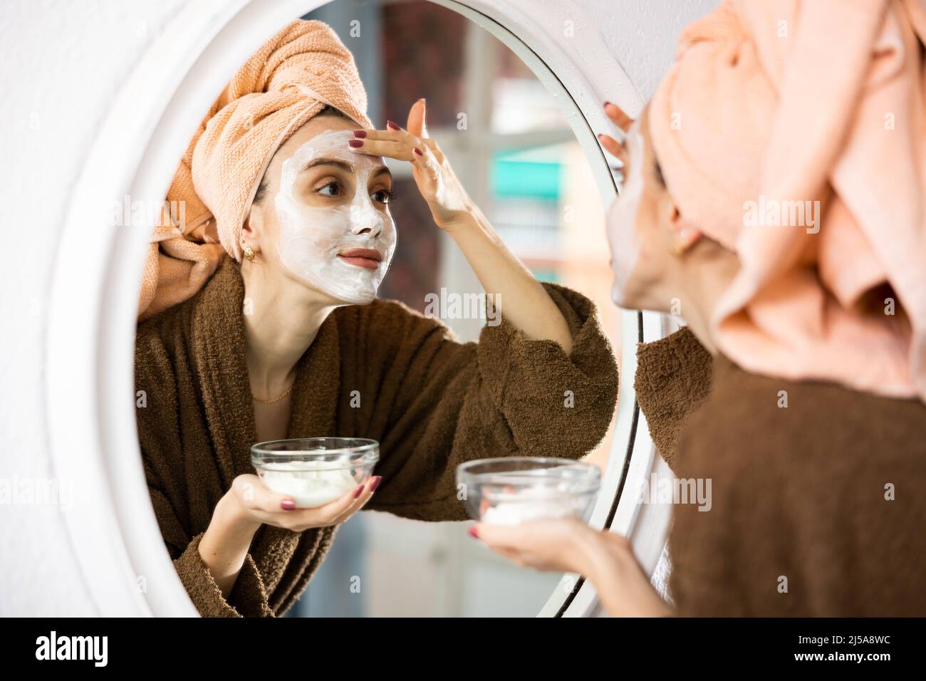Woman smoothing face cream in front of mirror Stock Photo - Alamy