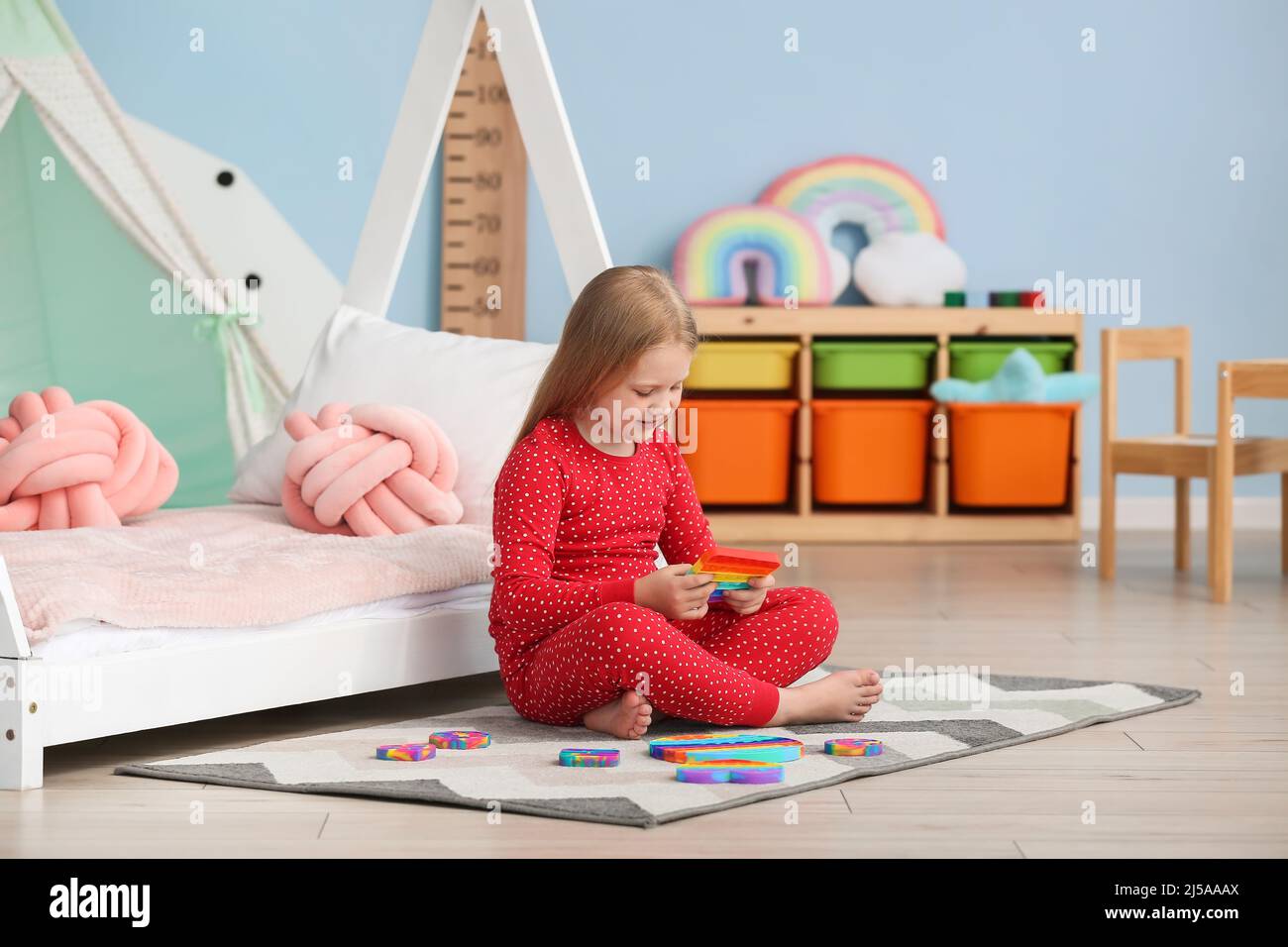 Pretty girl sitting on floor near bed and playing with pop it fidget ...