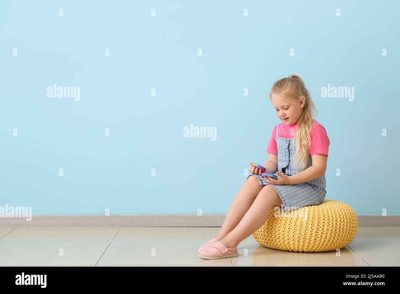 Pretty girl sitting on pouf and playing with pop it fidget toys near ...
