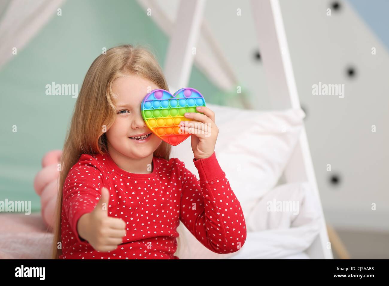 Girl showing thumb-up and holding heart shaped pop it fidget toy in ...