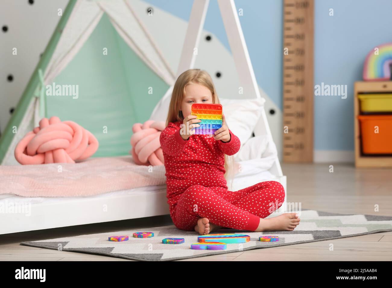 Little girl sitting on floor and holding multicolored pop it fidget toy ...