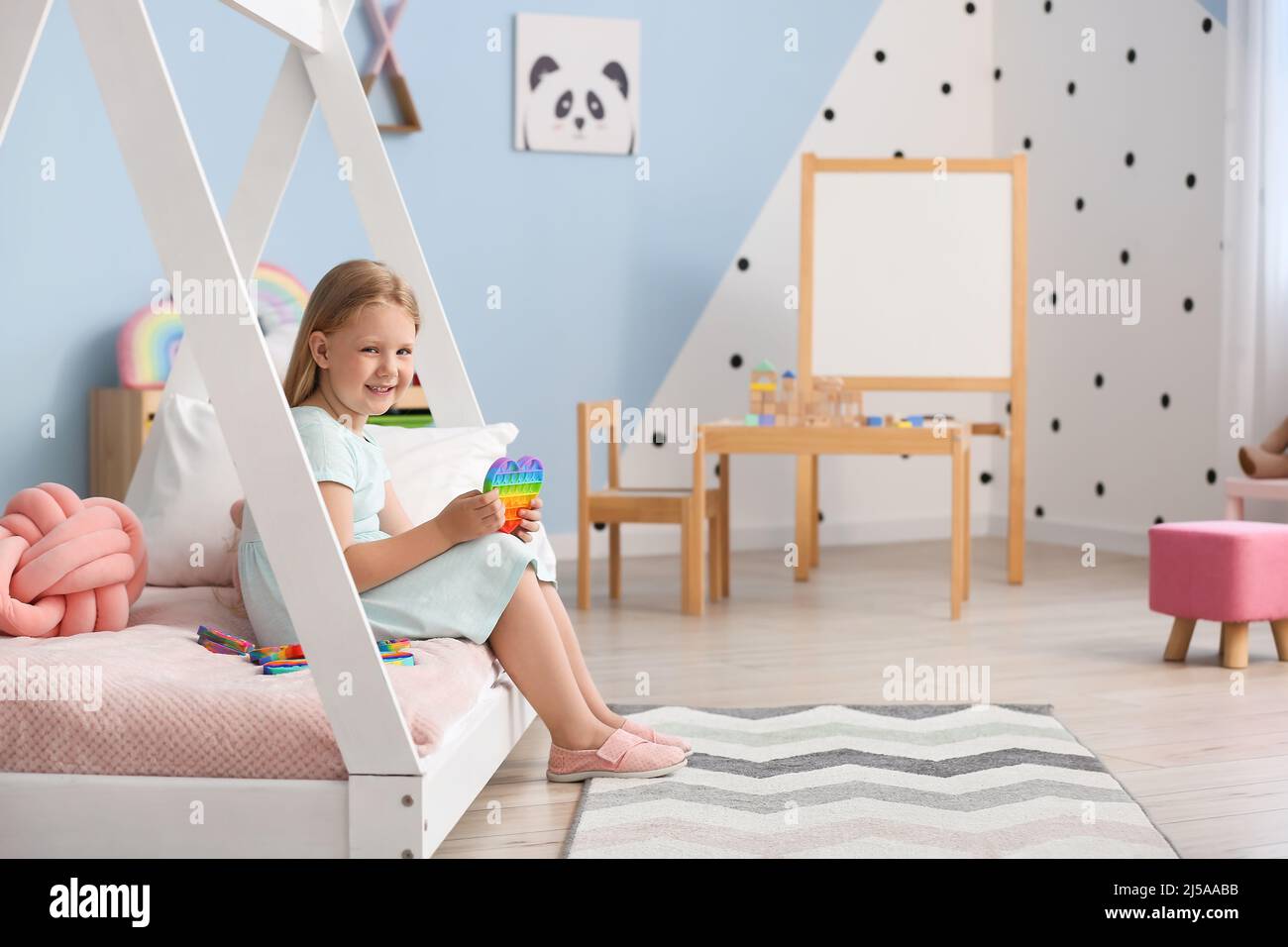 Happy little girl sitting on bed and playing with pop it fidget toy in ...