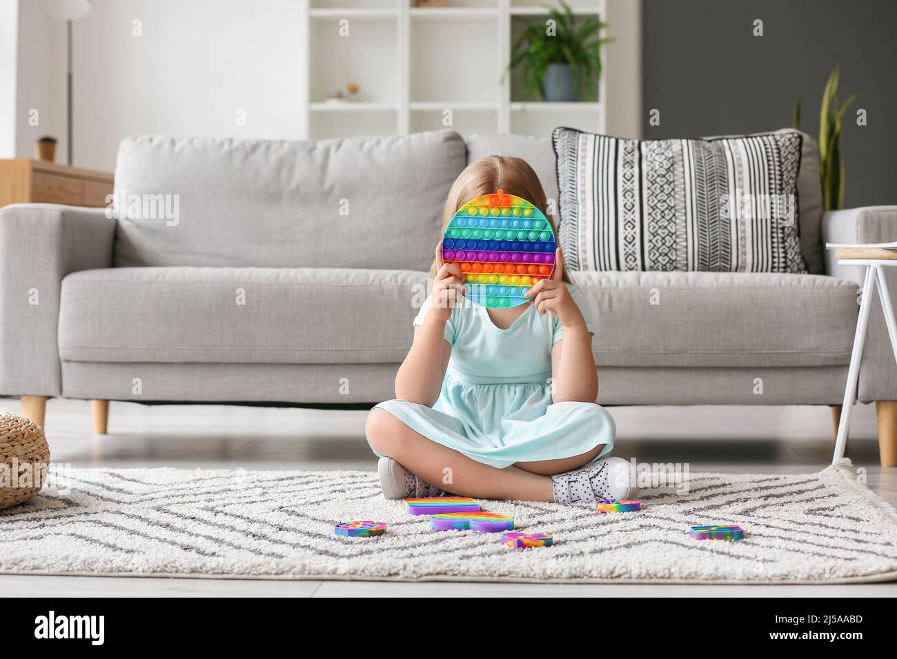 Little girl sitting on floor and holding multicolored pop it fidget toy ...