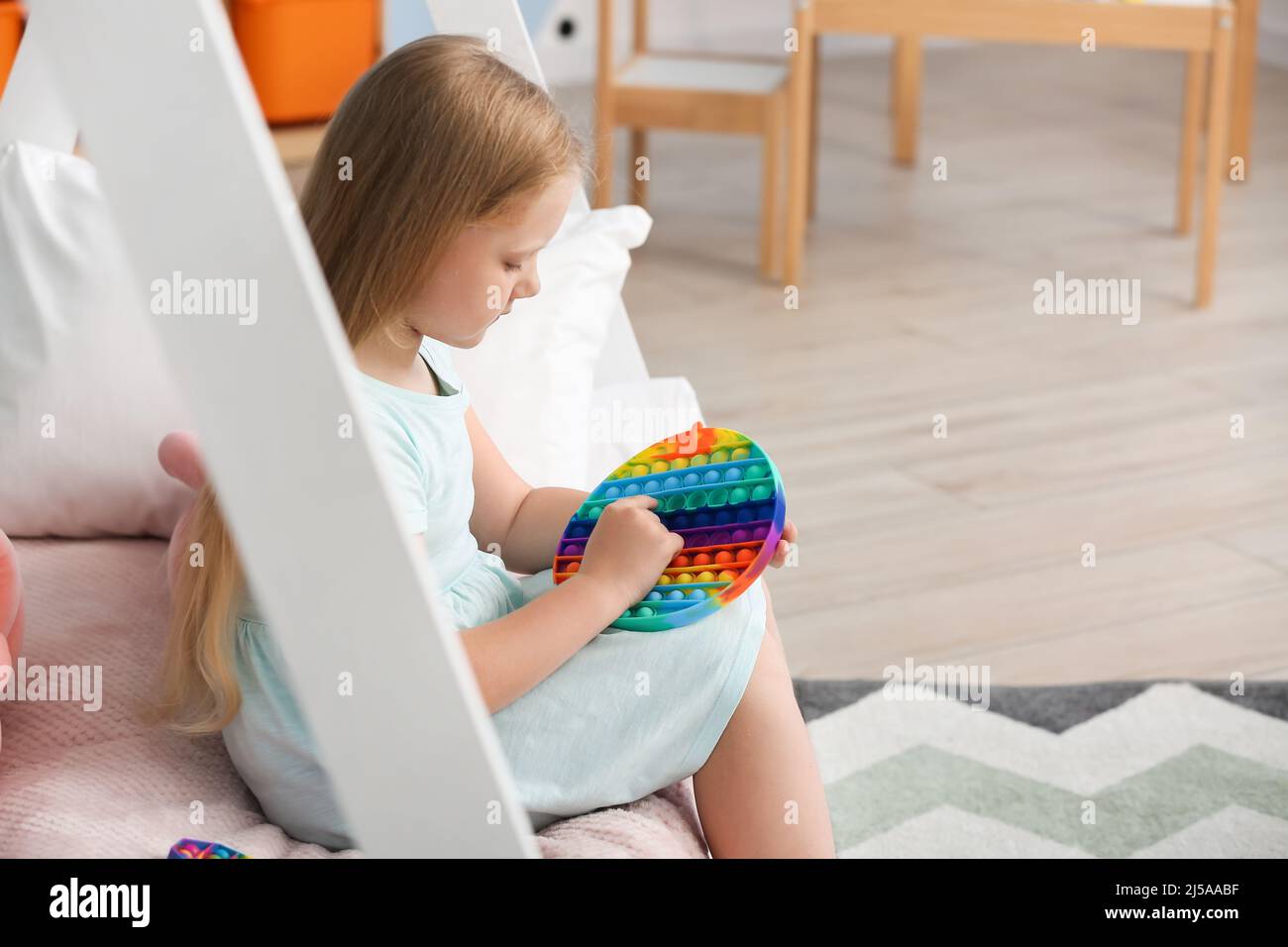 Girl sitting on bed and playing with pop it fidget toy in child room ...