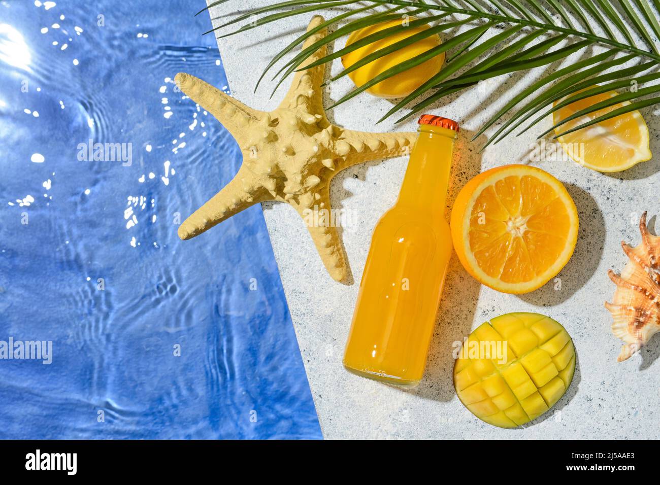 Bottle of tasty soda with fruits and sea shells near swimming pool ...