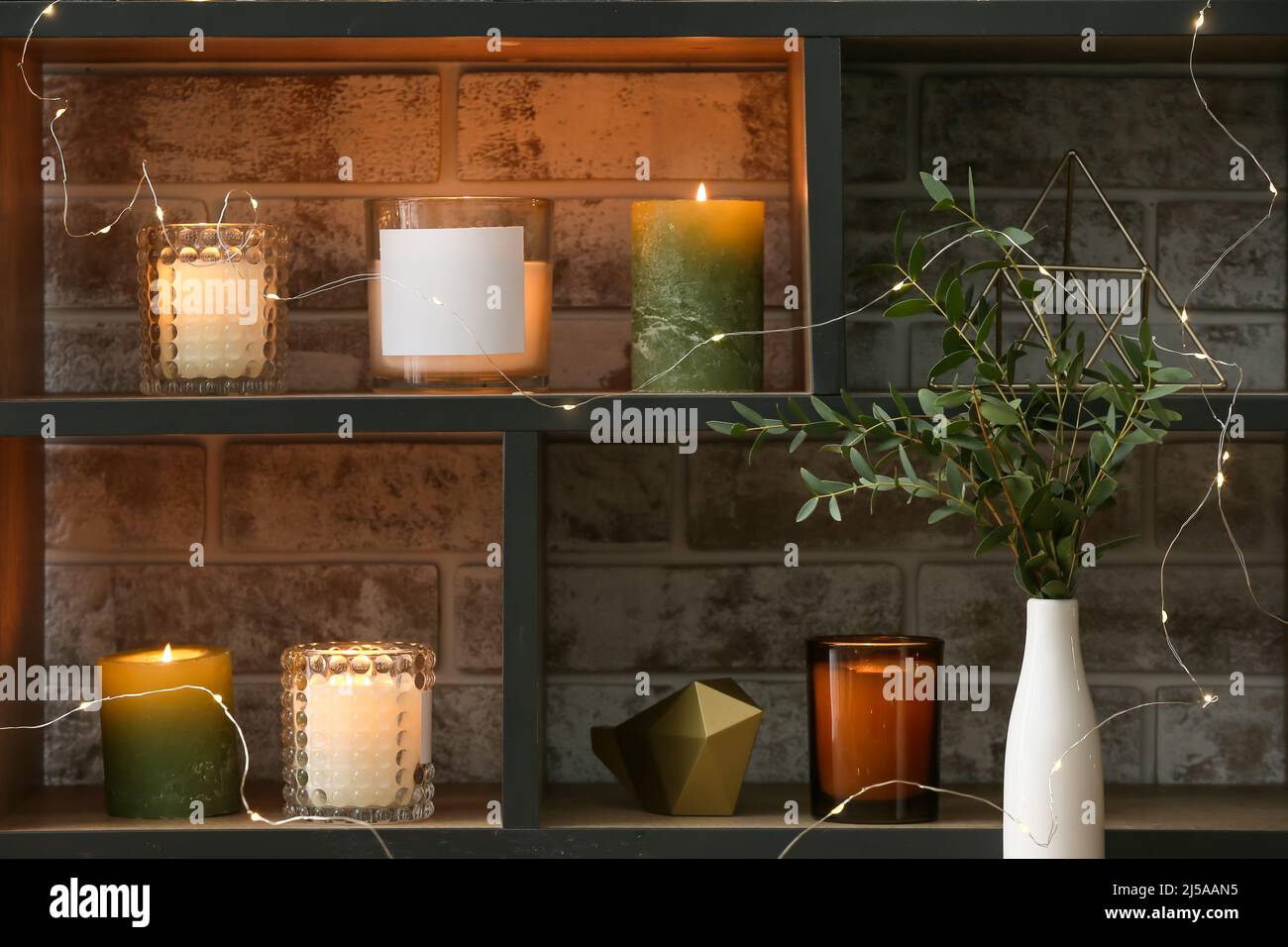 Holders with burning candles on shelf unit Stock Photo - Alamy