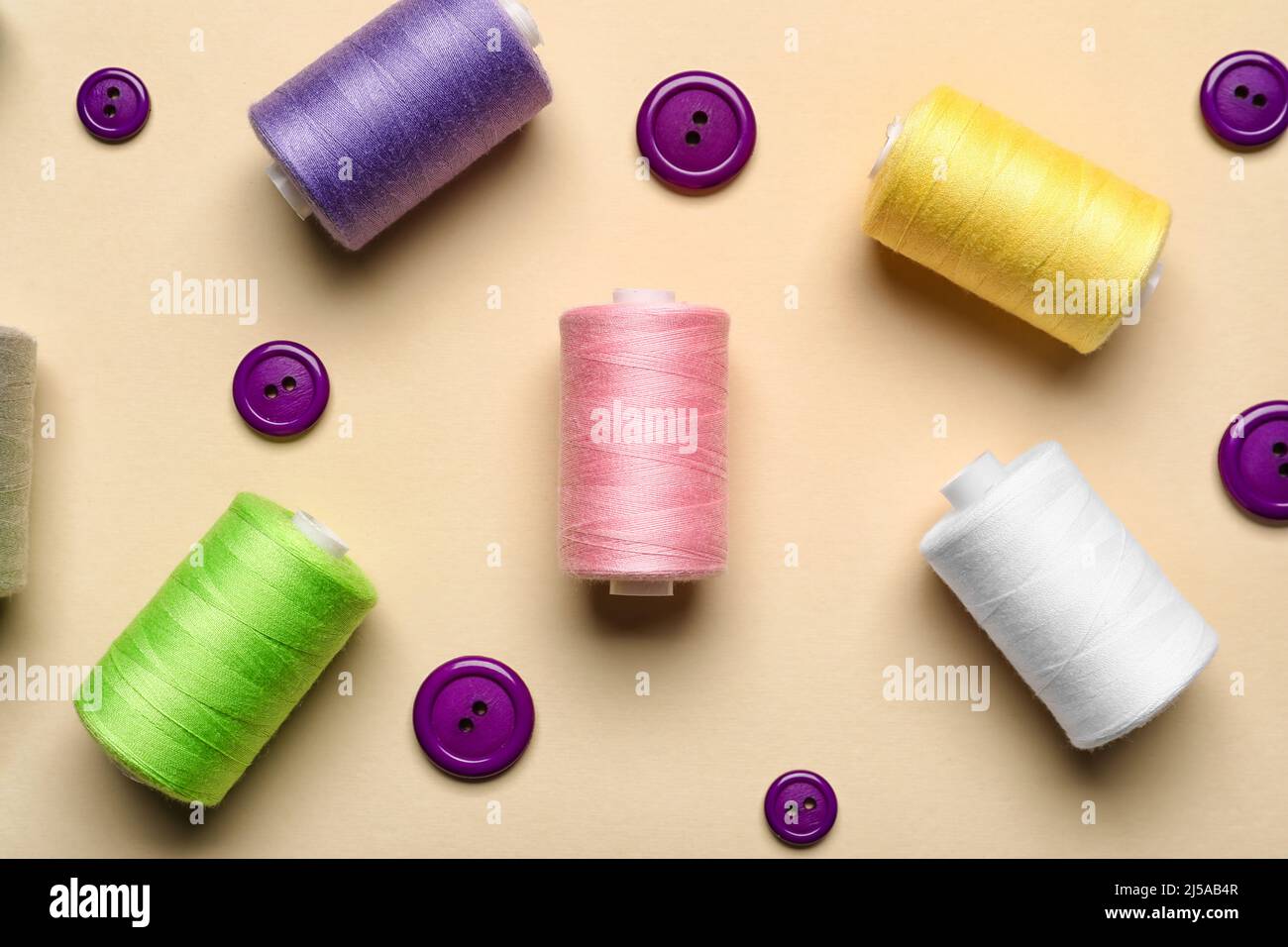 Sewing threads with buttons on beige background Stock Photo - Alamy