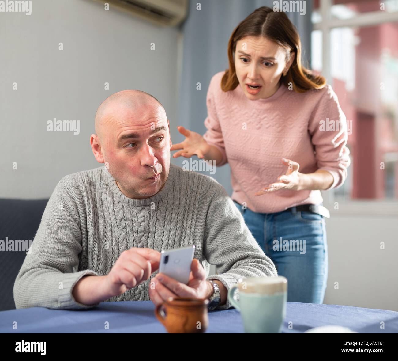 Angry wife observing her husband sitting and using phone Stock Photo ...