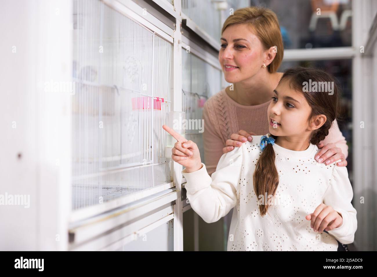 Girl with her mother buying bird in pet store Stock Photo - Alamy