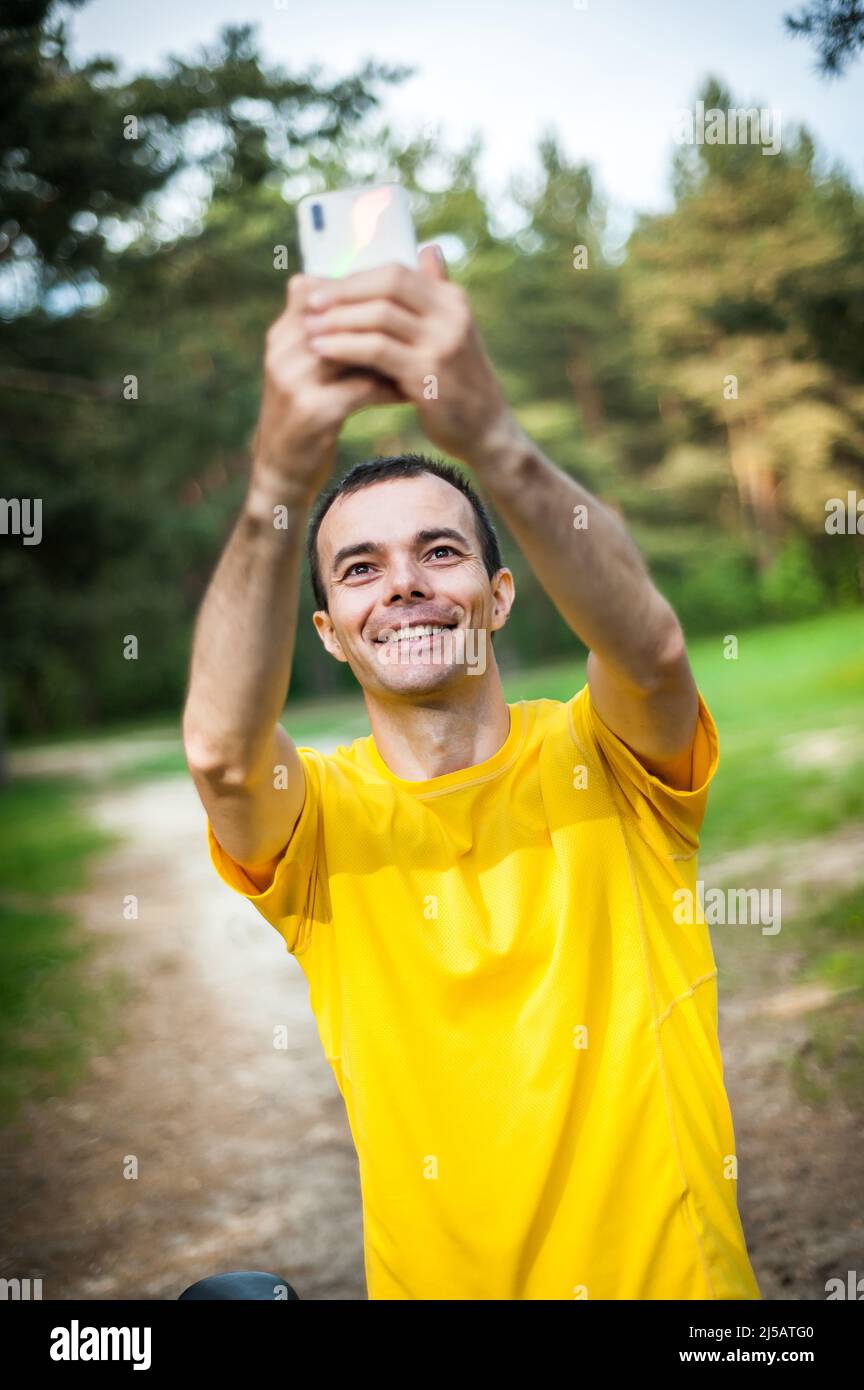 A young man taking a selfie with his Bicycle. In a public Park, among ...